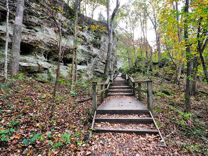 Autumn leaves carpet the trail as wooden steps climb toward rock formations that have stood for thousands of years.