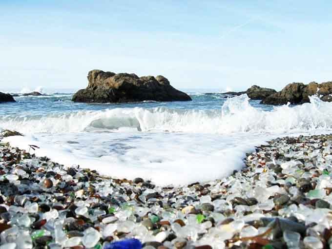 Waves wash over a beach made entirely of polished glass, sparkling like scattered jewels.
