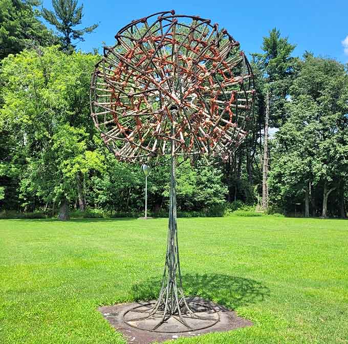 An intricate metal flower blooms eternally, its delicate framework creating lacy patterns against the summer sky above.