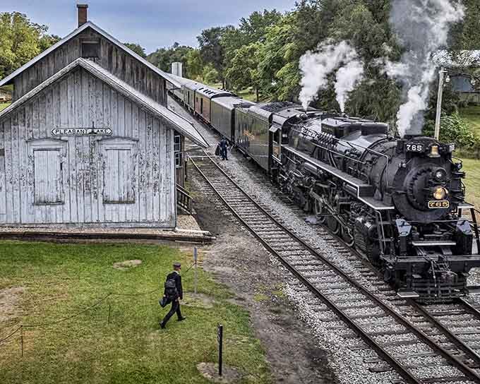 Steam billows dramatically as the locomotive passes weathered buildings, creating a scene worthy of any history book.