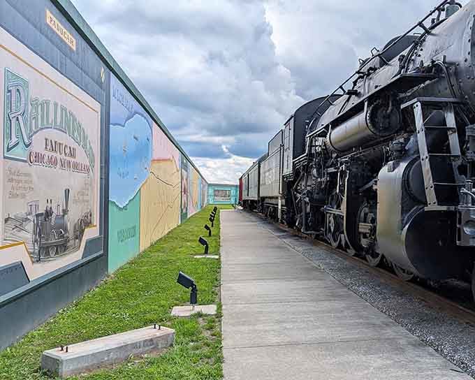 The vintage locomotive stands proud beside painted panels, connecting past and present in one powerful outdoor gallery experience.