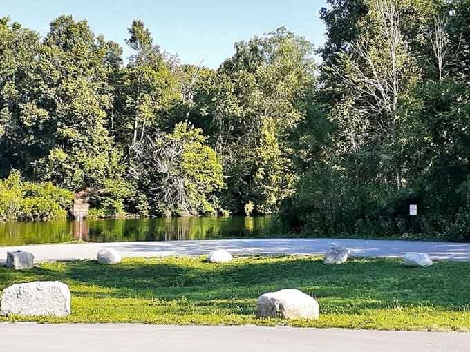 Where the river meets the road, tranquil waters mirror the trees in perfect summer stillness.