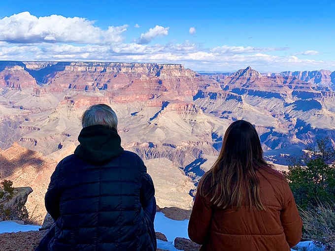 Two friends share nature's grandest theater, bundled against winter's chill while absorbing timeless canyon views.