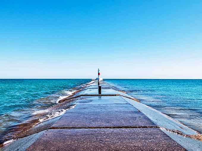 This concrete pier stretches toward the striped beacon like a runway, waves lapping rhythmically on both sides below.