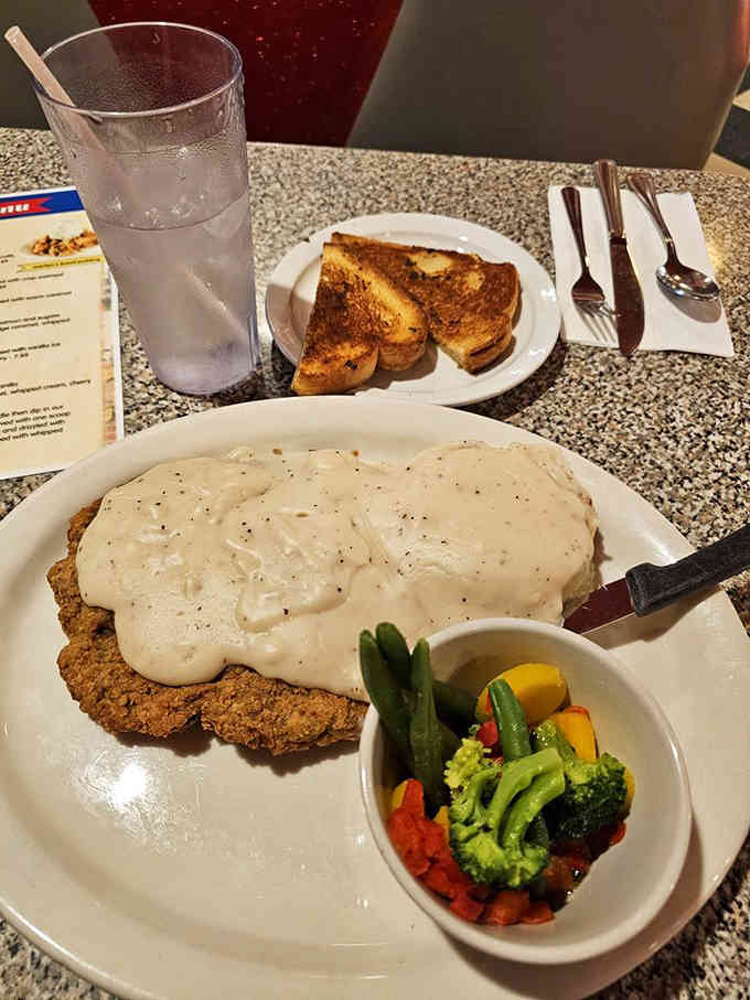 Chicken fried steak drowning in country gravy alongside fresh vegetables represents the diner's commitment to hearty portions.