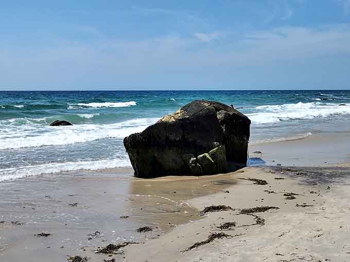 A lone boulder sits on pristine sand where turquoise waves meet shore in perfect coastal harmony.