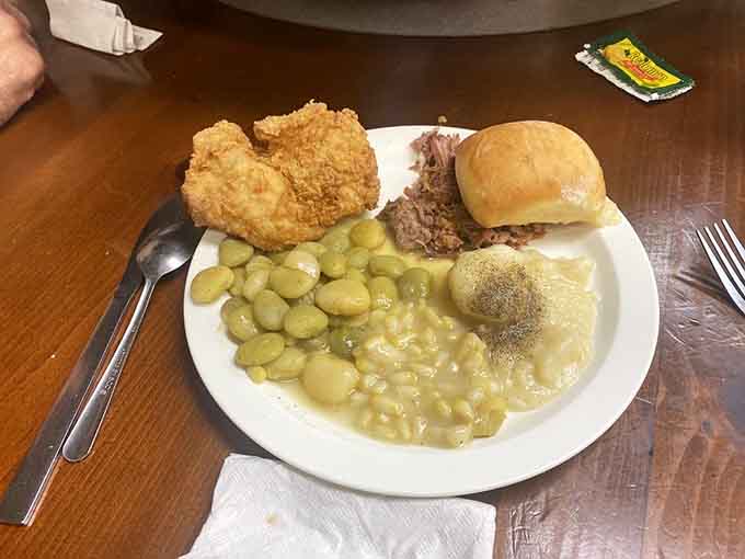 A plate loaded with fried chicken, butter beans, mac and cheese, and rolls represents Southern hospitality in its most delicious form.
