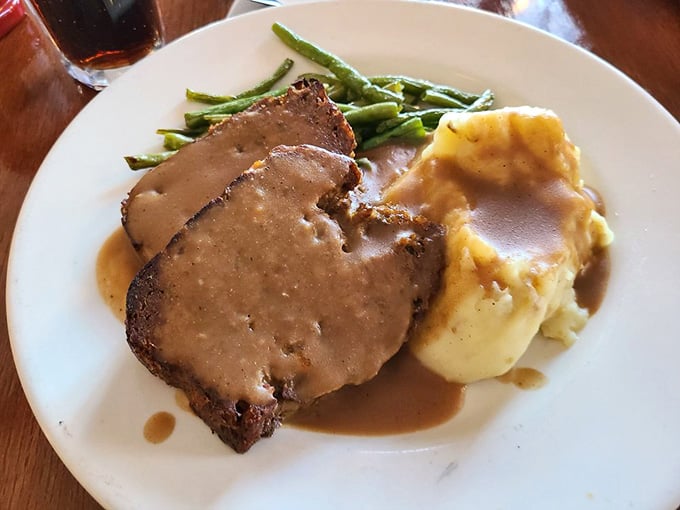 Sliced meatloaf with gravy cascading over mashed potatoes, proving simple done right beats fancy done wrong.