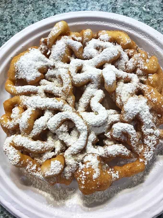 Funnel cake dusted with powdered sugar like fresh snow, the kind of dessert that makes napkins completely pointless.