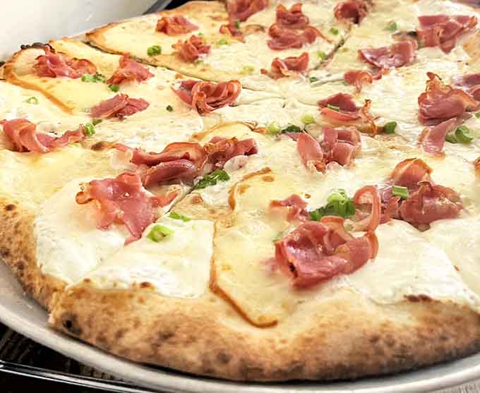 Prosciutto draped over creamy white pizza like silk scarves on fresh snow, utterly elegant.