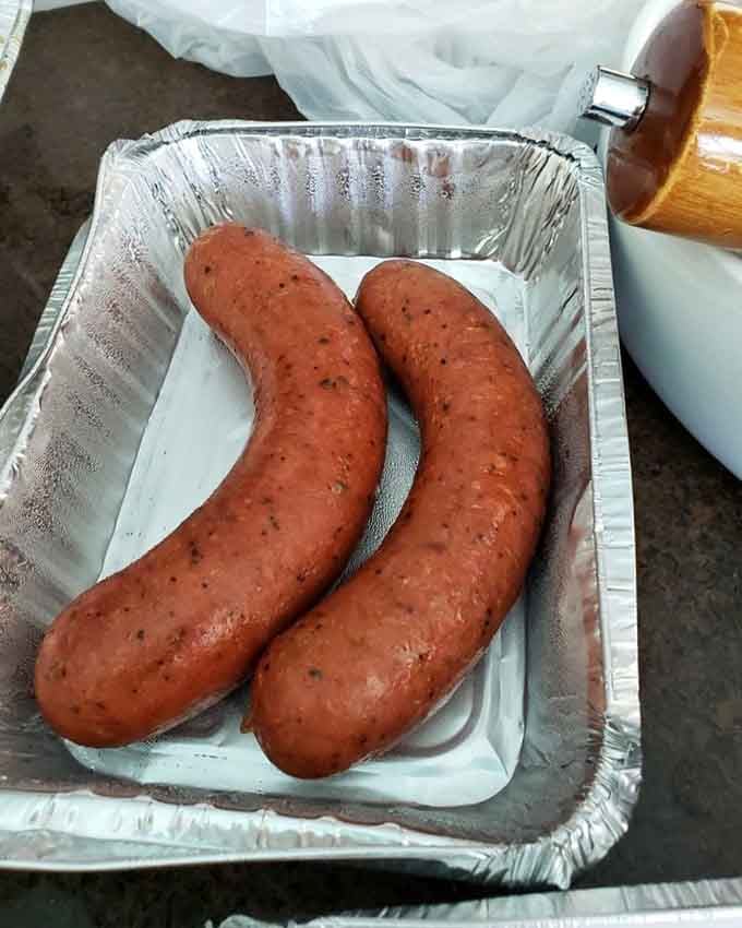 Two perfectly smoked sausages resting in their aluminum throne, ready to deliver smoky, juicy satisfaction with every bite.