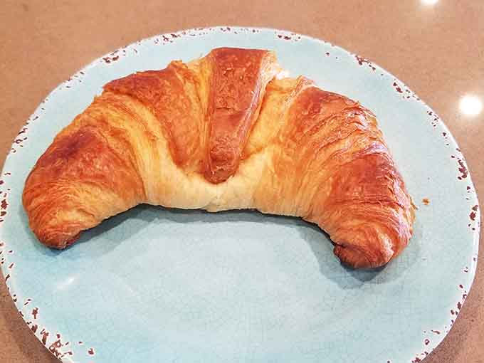 A croissant so beautifully laminated it could teach a masterclass, sitting pretty on its blue throne of deliciousness.