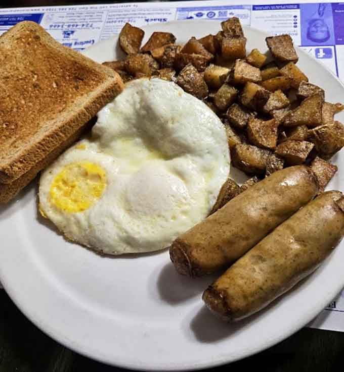 A perfectly fried egg alongside golden home fries and sausage links proves simplicity done right wins every time.