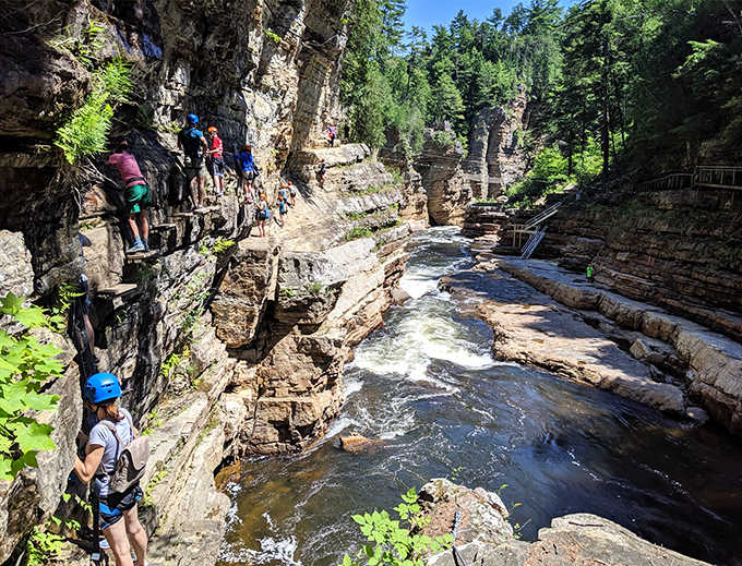 Narrow rock passages tower overhead as adventurous souls navigate the gorge trail, Indiana Jones style but with better safety rails.