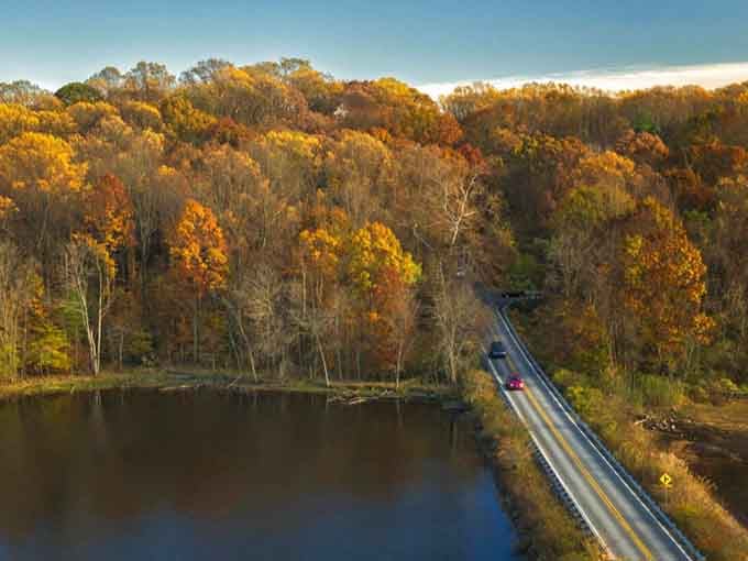 This aerial view reveals how the road hugs autumn-kissed forests like a gentle embrace along the water.