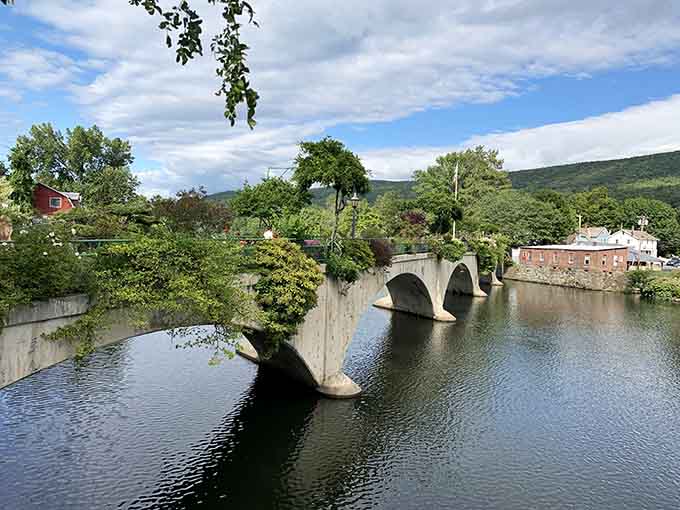 That graceful stone bridge spans calm waters with mountain views beyond, connecting two riverbanks in timeless New England style.