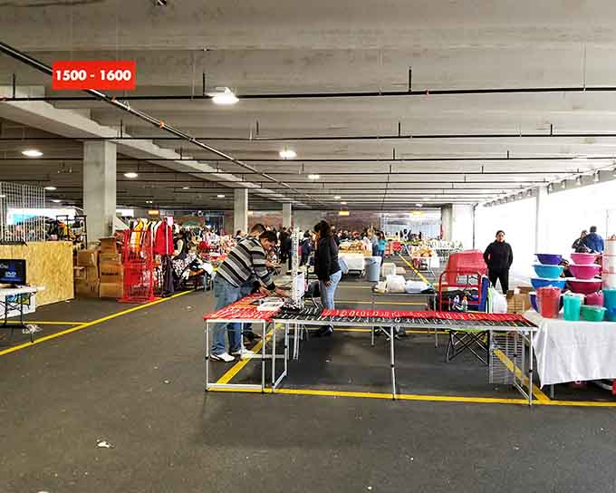 Underground parking transforms into a bustling marketplace where fluorescent lights illuminate tables packed with colorful merchandise and possibilities.