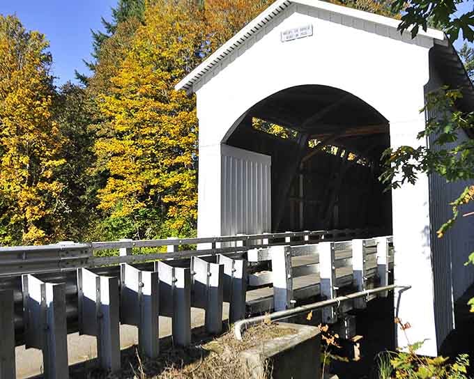 Golden autumn leaves frame this classic covered bridge, white paint gleaming against the fall colors beyond.