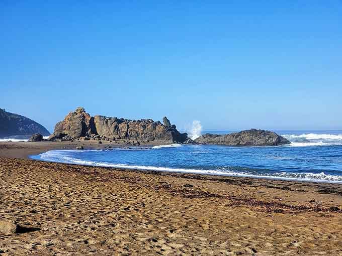 Golden sand meets crashing surf while rocky outcrops stand guard like ancient sentinels on permanent beach duty.