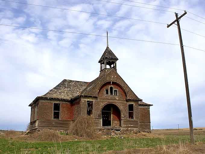 The arched entrance and bell tower still stand proud despite missing windows, like a patient sentinel on the windswept prairie.