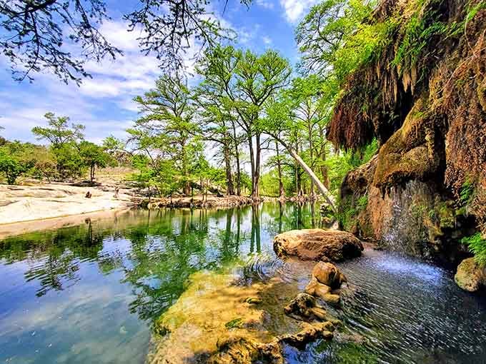 Spring water trickles down the rock face, creating natural pools surrounded by cypress trees and pure serenity.