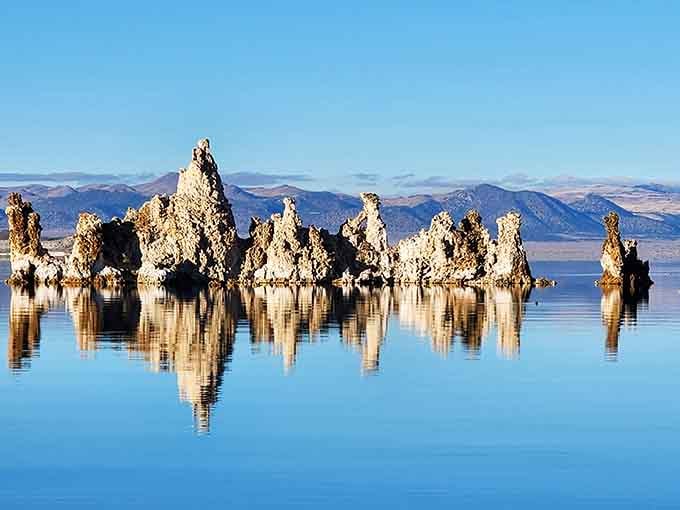 Limestone towers emerge from the alkaline water like melting sculptures, their white forms reflected perfectly in the mirror-smooth lake.