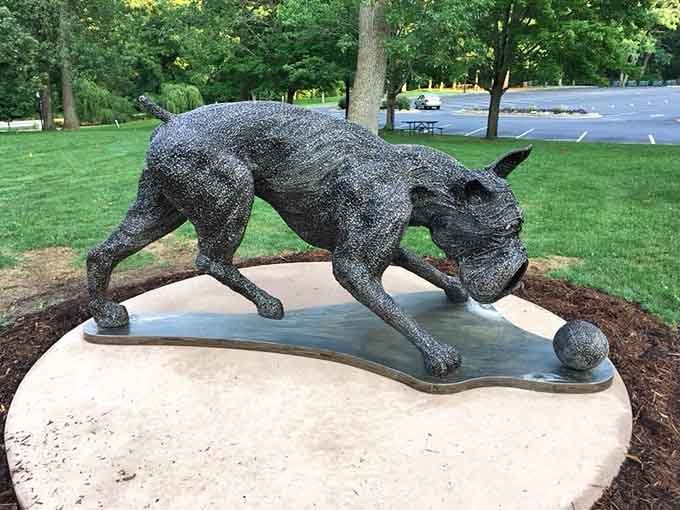 This playful cat sculpture crouches low, forever stalking an invisible prey across its concrete platform with focused intensity.