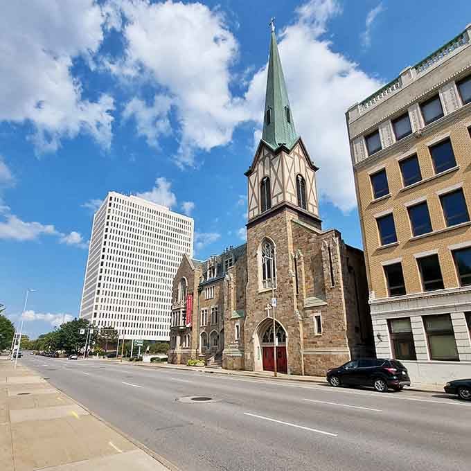 The copper-green steeple pierces blue sky between old and new architecture, showing how cities grow without forgetting themselves.