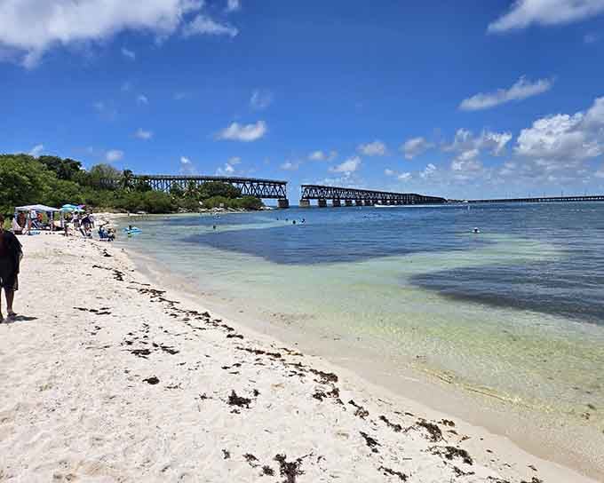 The old railroad bridge stands sentinel over paradise where shallow waters invite swimmers into liquid gemstone beauty.