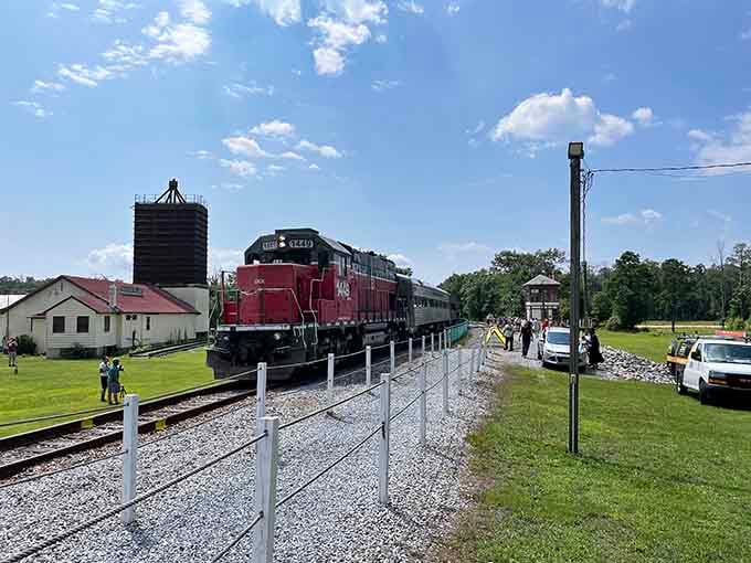 The burgundy diesel leads its train through open farmland where blue skies meet endless green horizons.