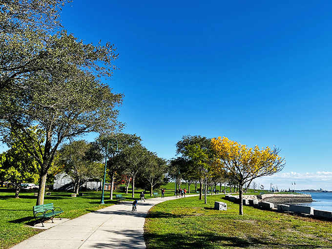 Tree-lined paths curve along the waterfront, offering perfect spots for strolling while sailboats drift past like floating daydreams.