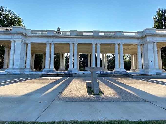 Afternoon light streams through the colonnade, casting geometric patterns that dance across the peaceful park grounds.