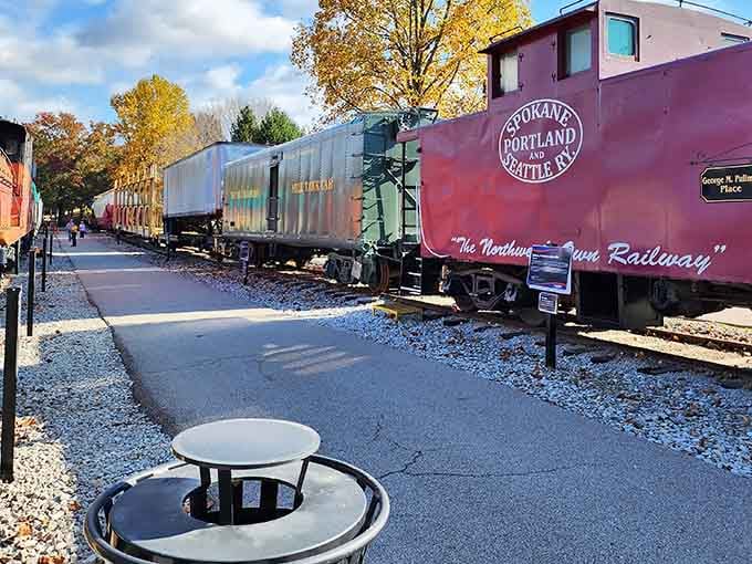 Autumn leaves frame the burgundy caboose perfectly, while golden foliage adds warmth to this nostalgic railway display scene.