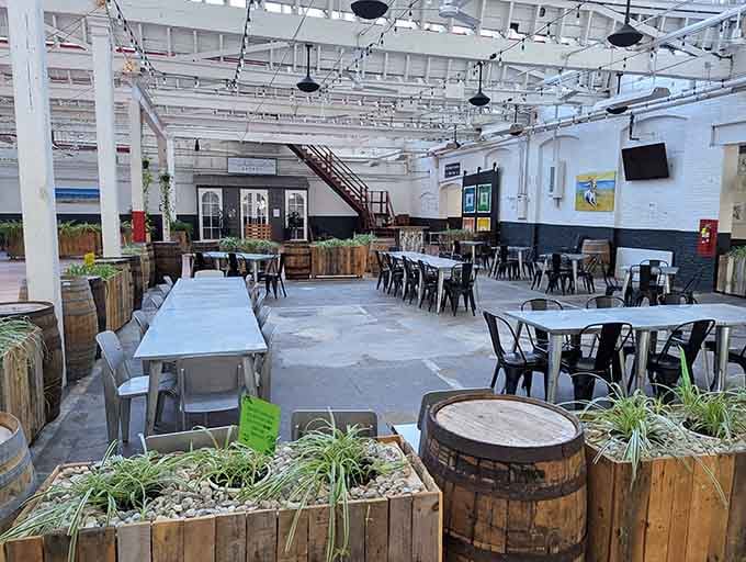 White-painted ceiling beams frame this airy space where rustic barrels and greenery soften the industrial warehouse vibe.
