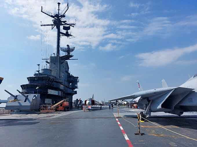The flight deck stretches like a small city, with vintage aircraft frozen in time under endless sky.