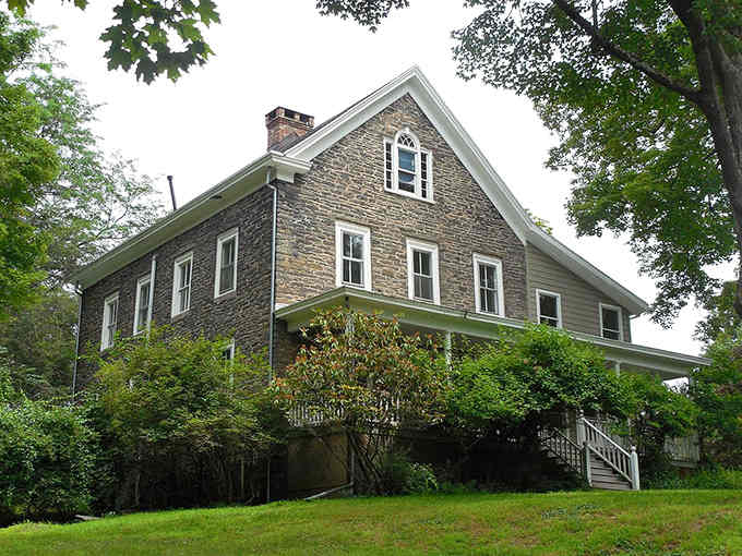 This stone house perches on a hillside surrounded by trees, looking like it's been keeping secrets since the Revolutionary War.