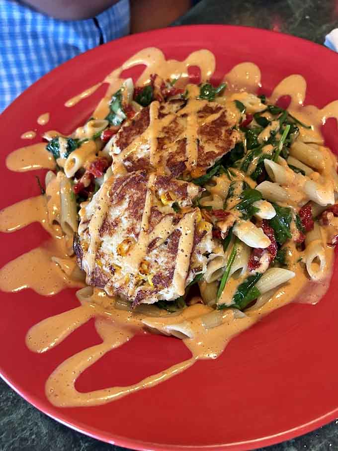 Golden crab cakes nestled in pasta with creamy sauce drizzled like edible art across the plate.