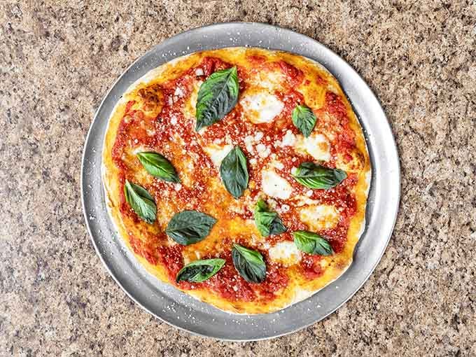 Fresh basil leaves crown this Margherita like tiny green flags of victory planted on a cheesy, saucy landscape.