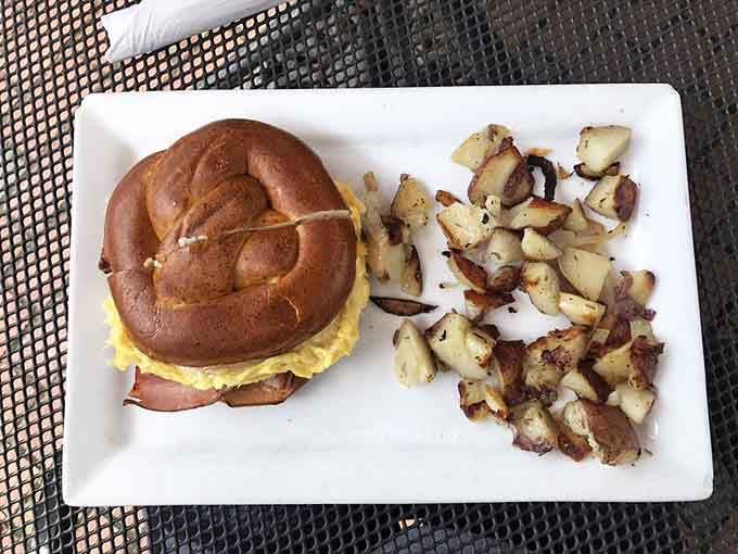 The German on a pretzel roll with crispy home fries delivers the kind of breakfast that makes you reconsider your entire morning routine.
