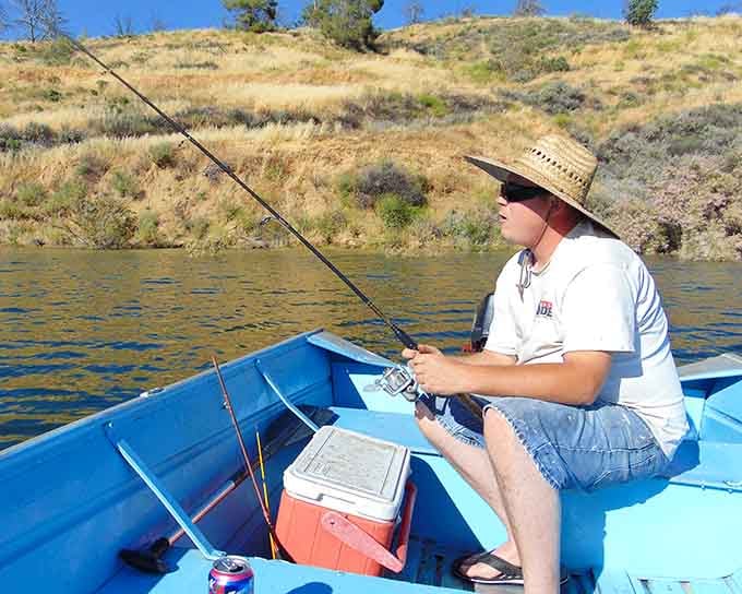 That straw hat says this angler means business, patiently waiting for the big one in his trusty blue boat.