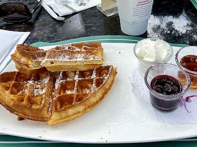 Belgian waffles dusted with powdered sugar and jam options, basically breakfast's greatest hits album on one plate.