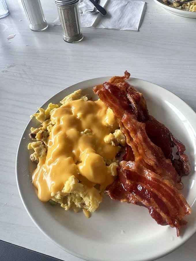 Fluffy scrambled eggs topped with melted cheese next to crispy bacon strips make mornings worth waking up for, honestly.