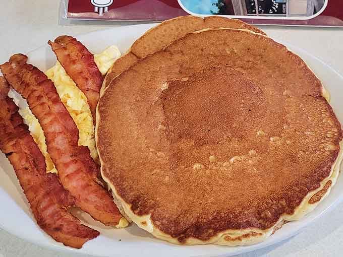 That pancake could double as a plate itself, flanked by bacon and eggs like bodyguards protecting royalty.