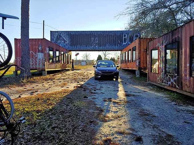 Weathered paint and afternoon light create shadows that dance across the gravel path leading to artistic discovery.