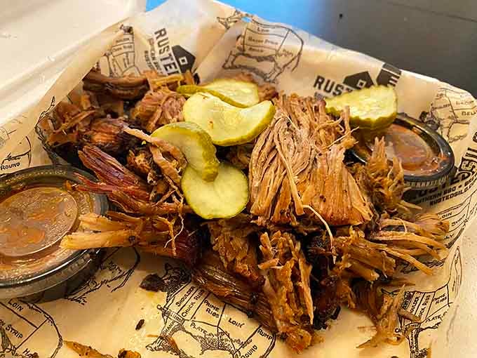 Pulled pork piled high with pickles and sauce cups standing by like loyal sidekicks ready for action.