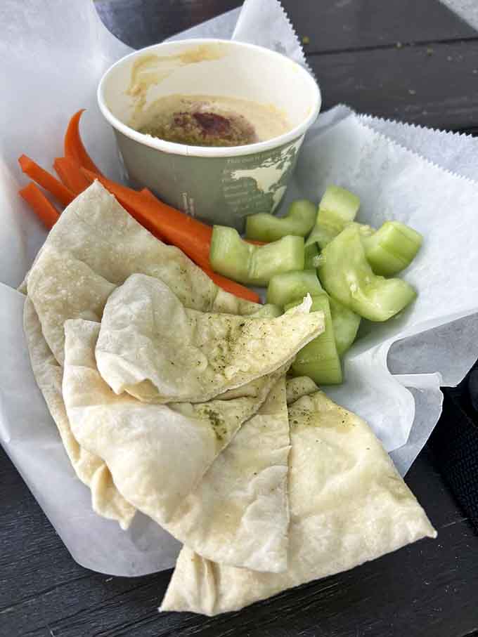 Fresh pita surrounds creamy hummus with colorful vegetables, offering lighter fare amidst all the delicious darkness surrounding you.