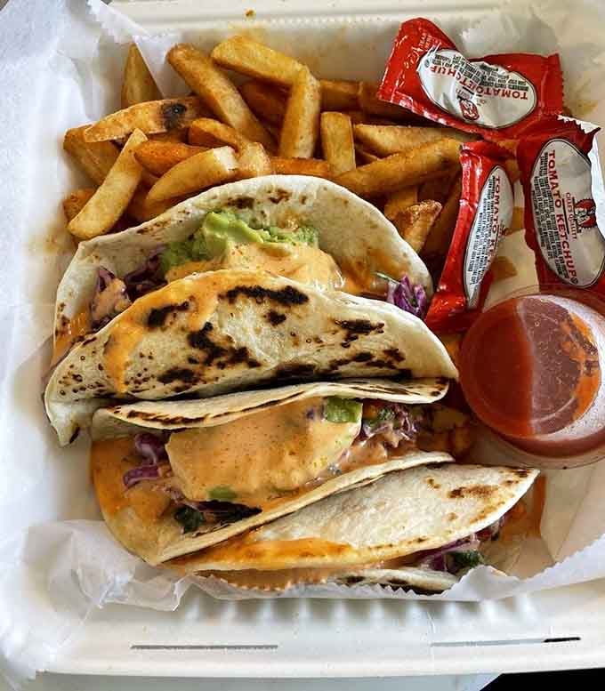 Fish tacos served with fries and hot sauce packets, because sometimes simplicity is the ultimate sophistication.