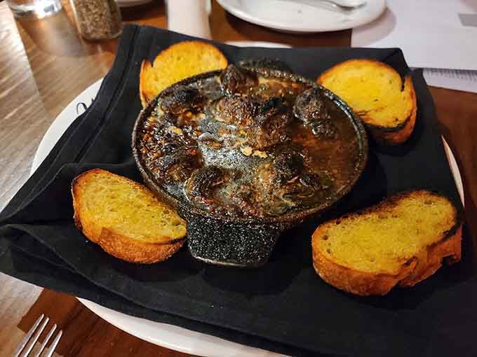 Escargot served sizzling in garlic butter with toasted bread for the perfect flavor delivery system.