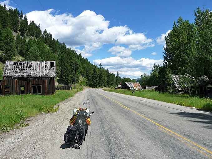 A lone cyclist pauses on the empty main street where false-front buildings lean precariously, frozen in their slow-motion collapse.