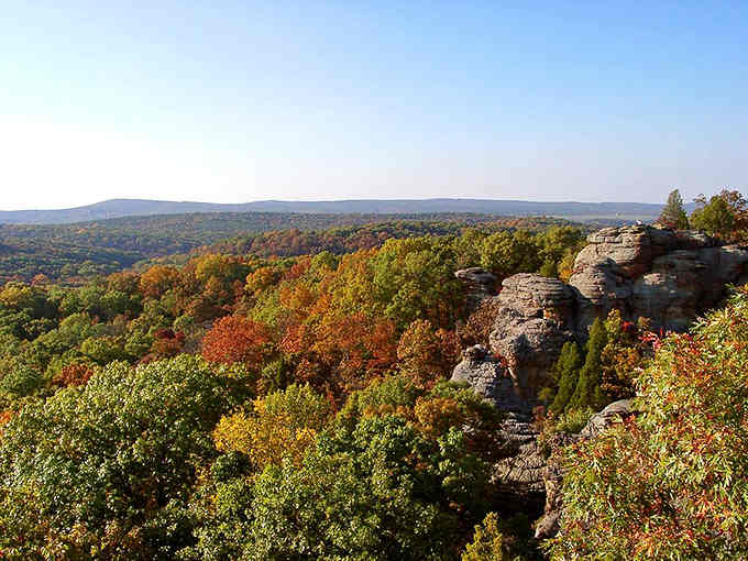 Fall colors paint the horizon in layers while weathered rock formations stand like nature's own sculpture garden below.